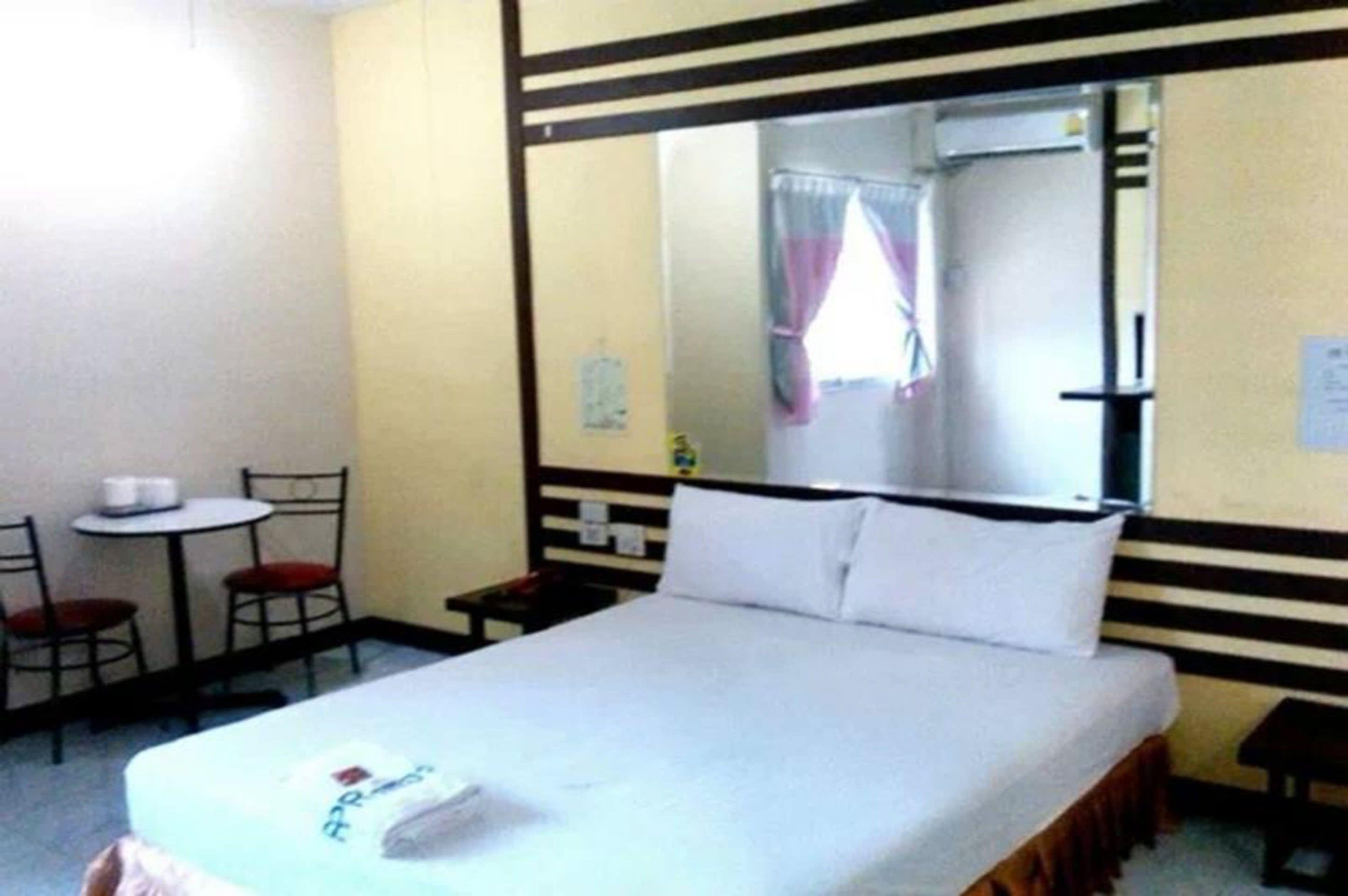Quarto de hotel com cama, uma pequena mesa com cadeiras, espelho e janela com cortinas.