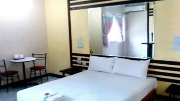 Quarto de hotel com cama, uma pequena mesa com cadeiras, espelho e janela com cortinas.
