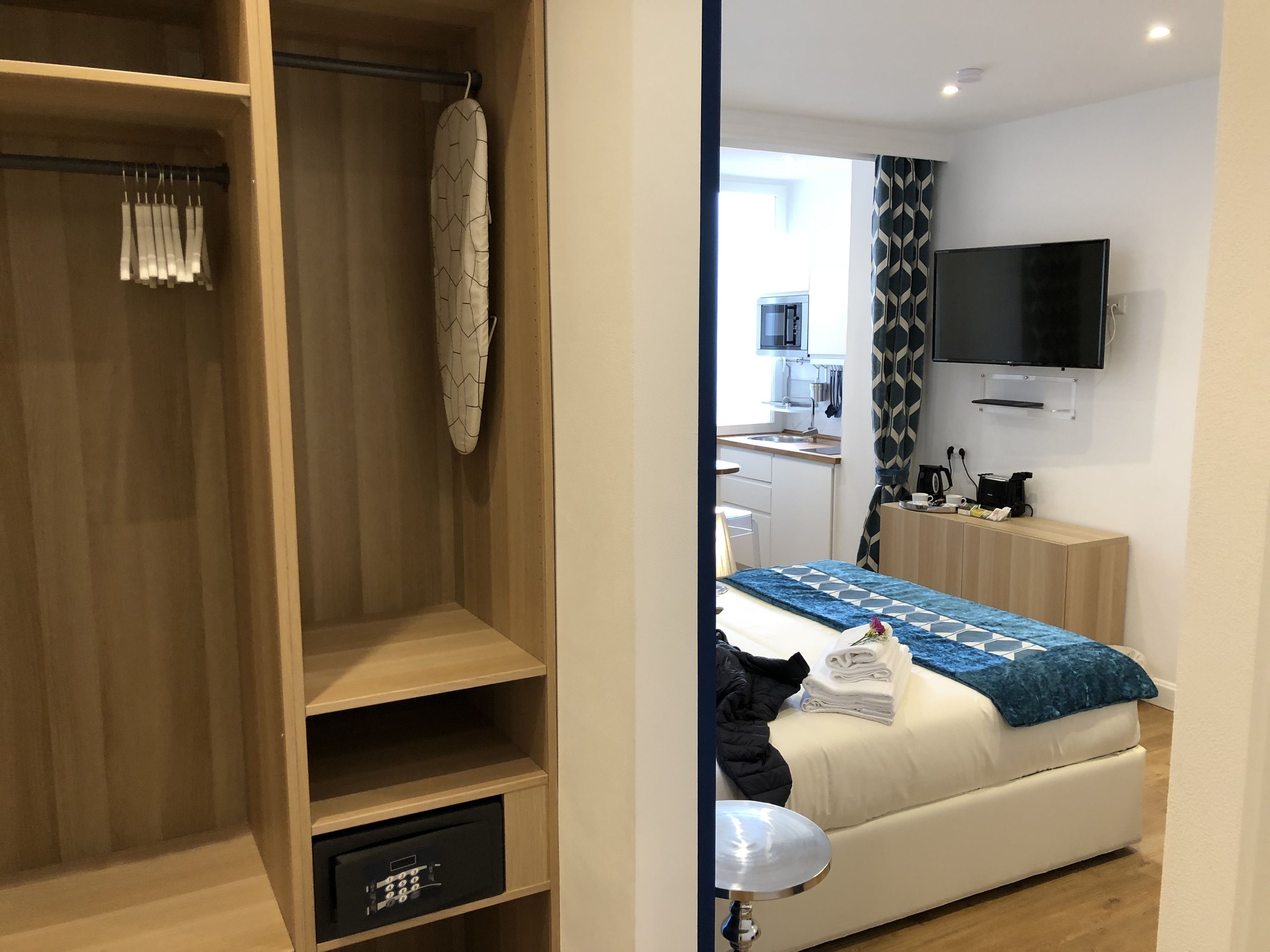 Quarto com cama, mesa de cabeceira, guarda-roupa e televisão na parede.