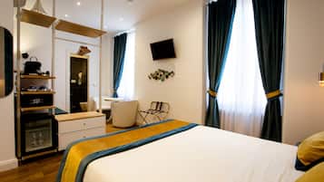 Quarto de hotel com cama, escrivaninha, cadeira, guarda-roupa e televisão na parede.