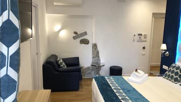 Quarto de hotel com cama, sofá, pequena mesa, unidade de ar condicionado, parede decorativa de pedra e luminária fixada na parede.