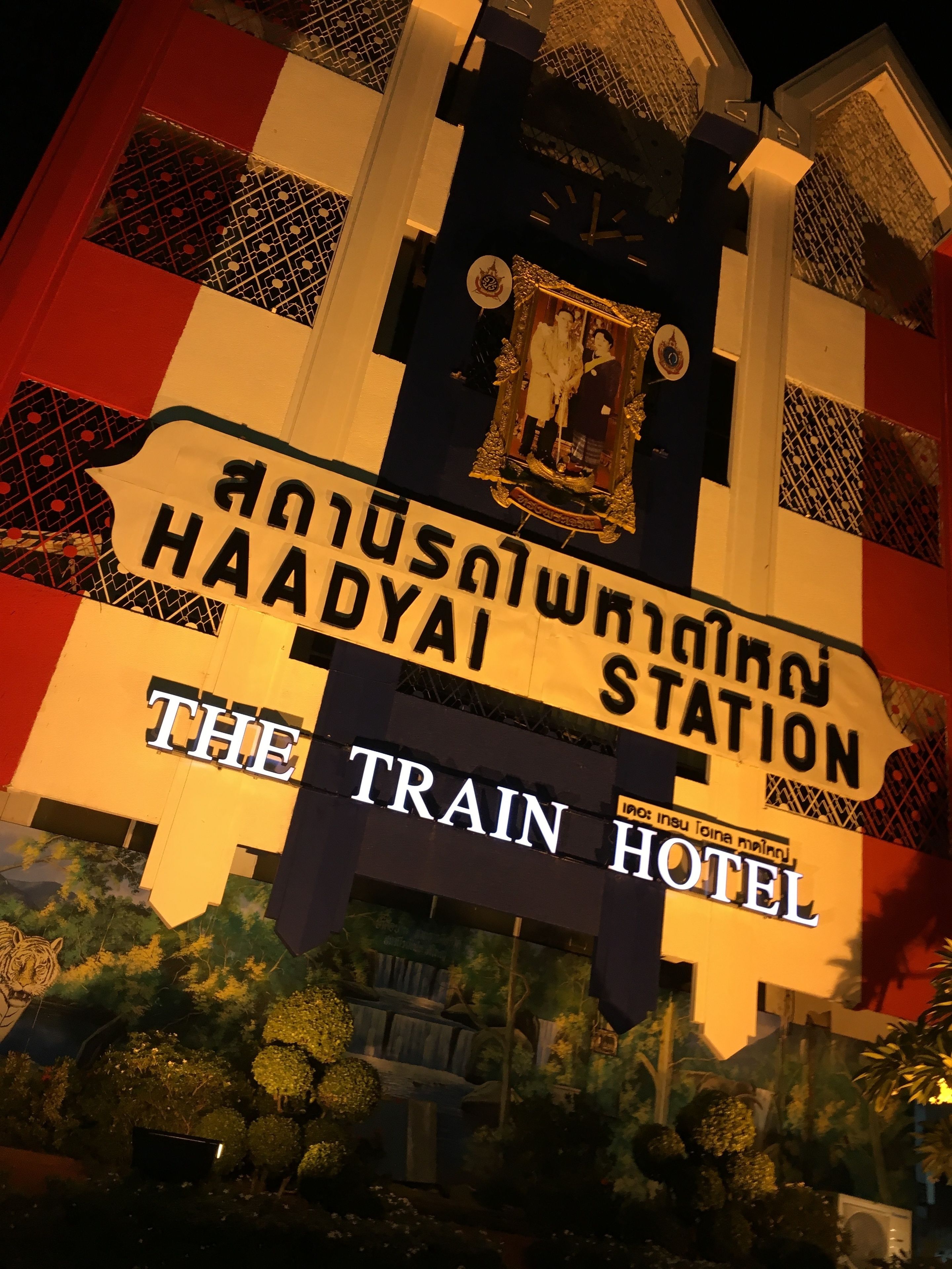 Placa do The Train Hotel com texto em tailandês e design arquitetônico tradicional tailandês.