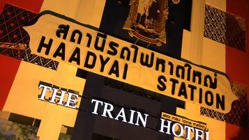 Placa do The Train Hotel com texto em tailandês e design arquitetônico tradicional tailandês.