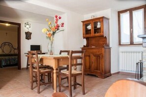 Uma sala de jantar com uma mesa e cadeiras de madeira, um armário e um vaso com flores.