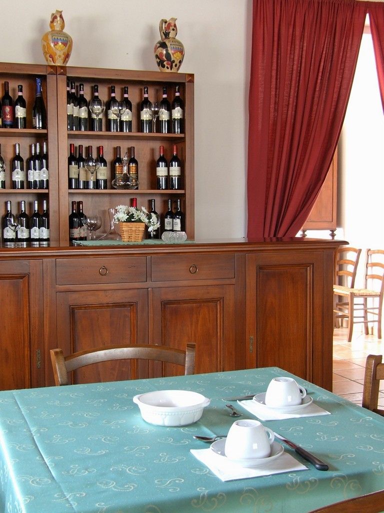 Uma sala de jantar com uma mesa posta para dois, um armário de madeira com garrafas de vinho e uma cortina vermelha.