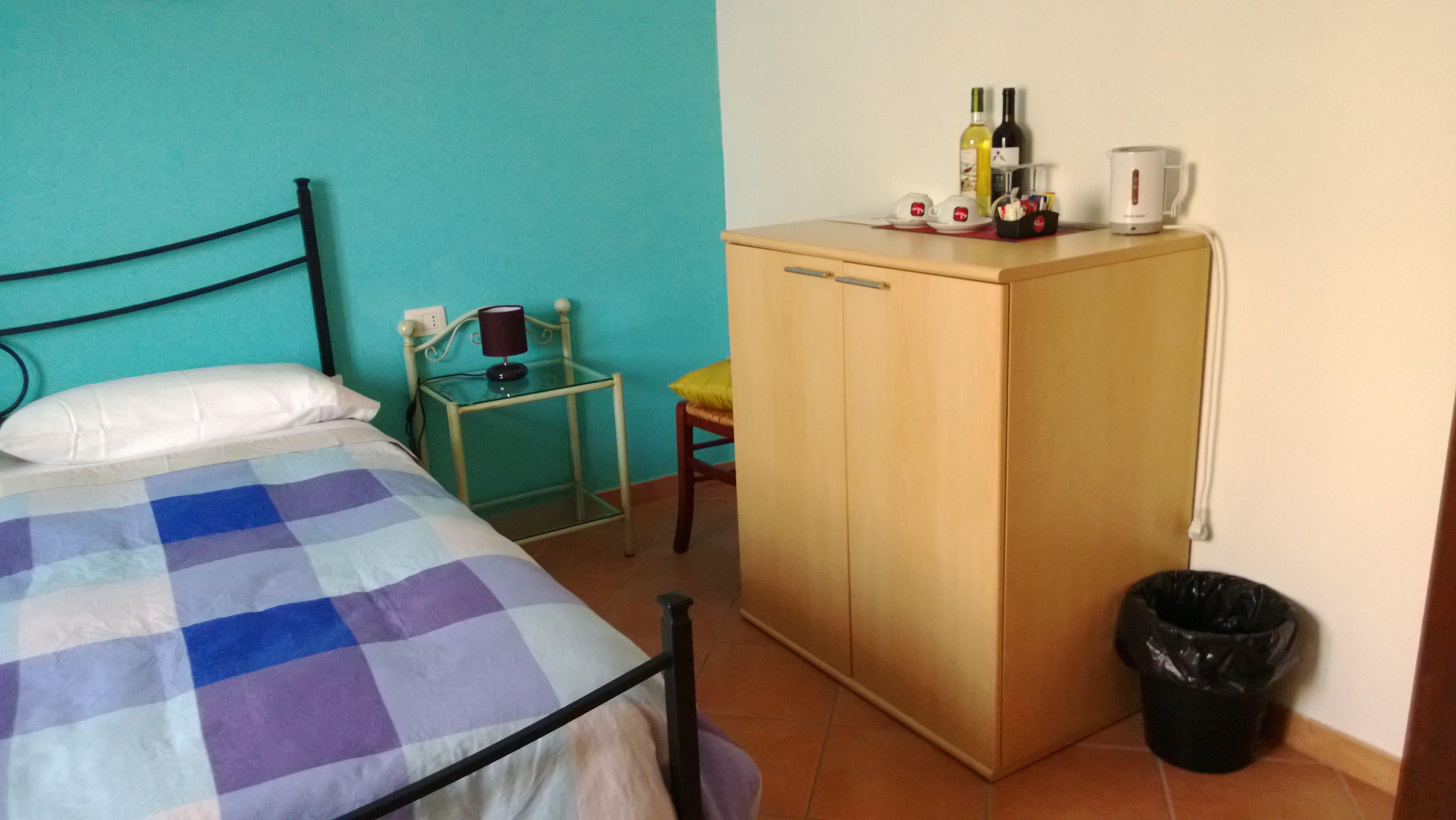 Um quarto com uma cama, mesa de cabeceira, armário pequeno, cadeira e lixeira.