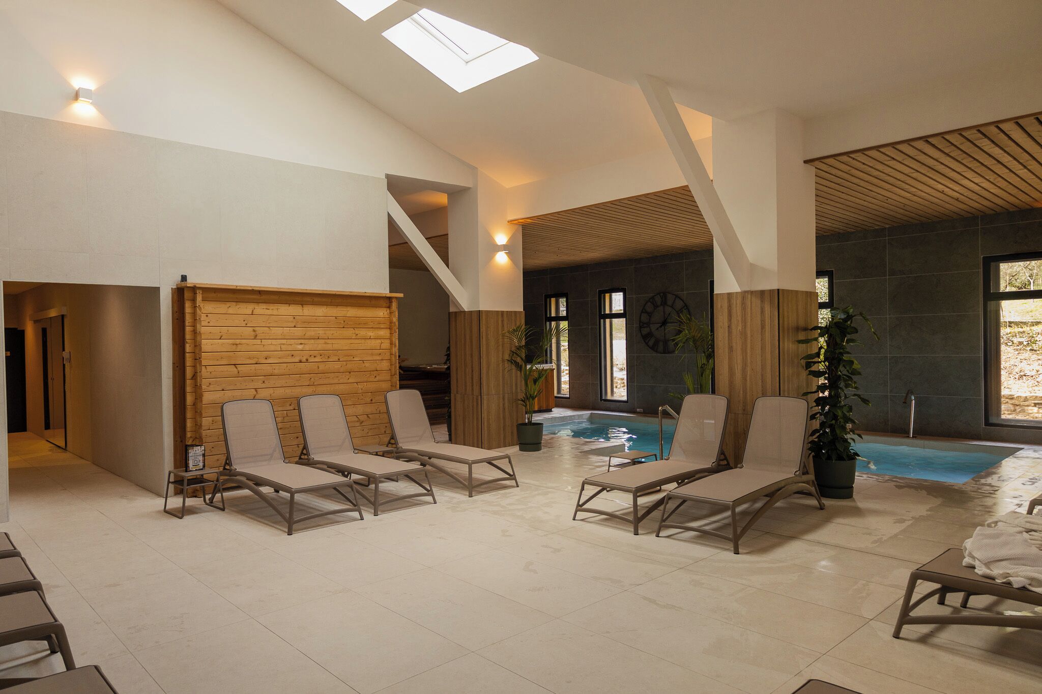 Espaçoso espaço interno com piscina, espreguiçadeiras, painéis de madeira e uma escada.