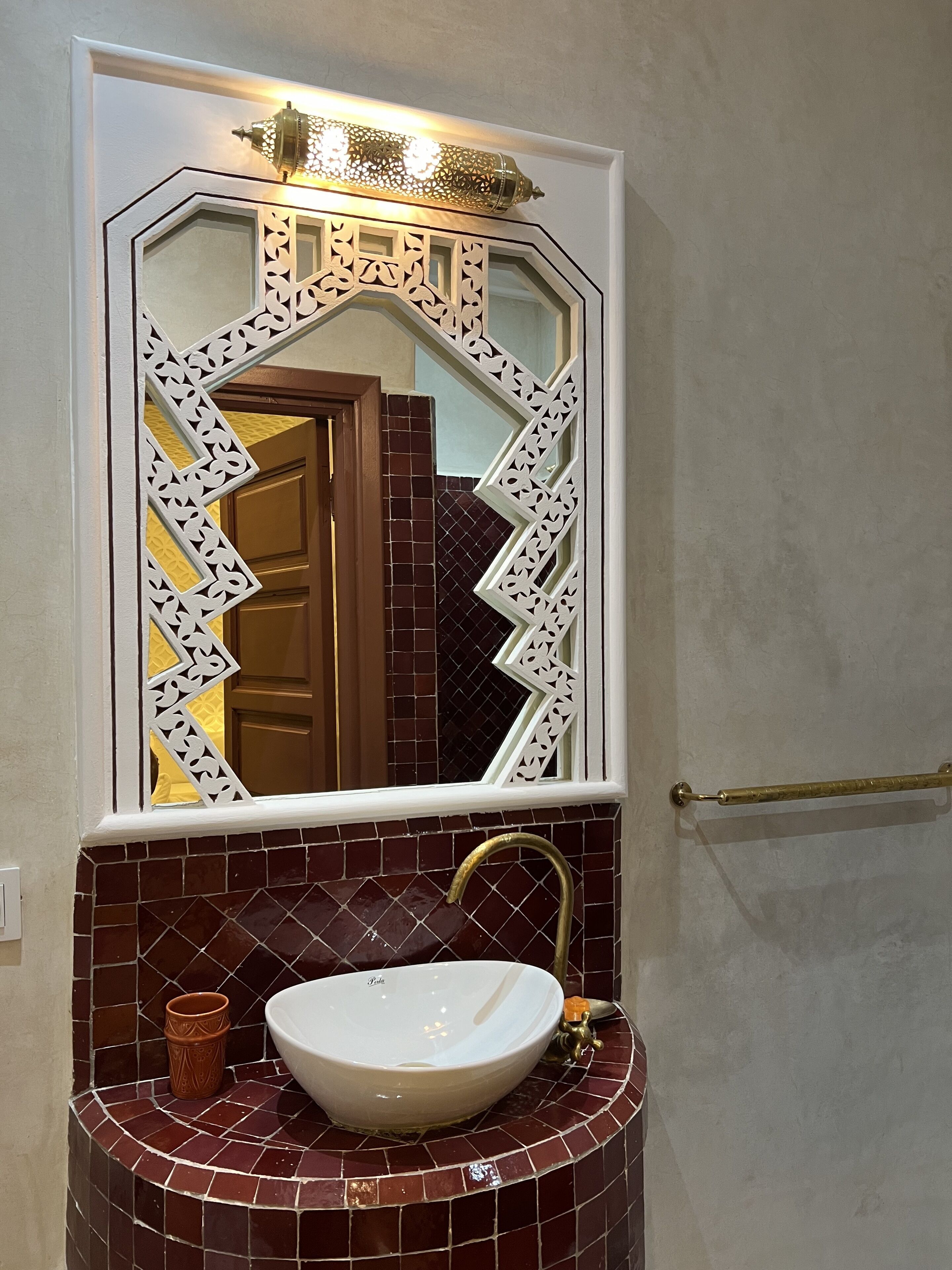 Um banheiro com pia branca, um espelho decorativo com moldura geométrica e um porta-toalhas fixado na parede.
