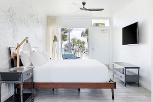 Quarto de hotel moderno com uma cama grande, escrivaninha, televisão de tela plana e varanda com vista para palmeiras.