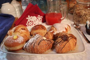 Um prato com diversos doces, incluindo donuts e croissants, uma guardanapo vermelha e um jarro de vidro com líquido vermelho.