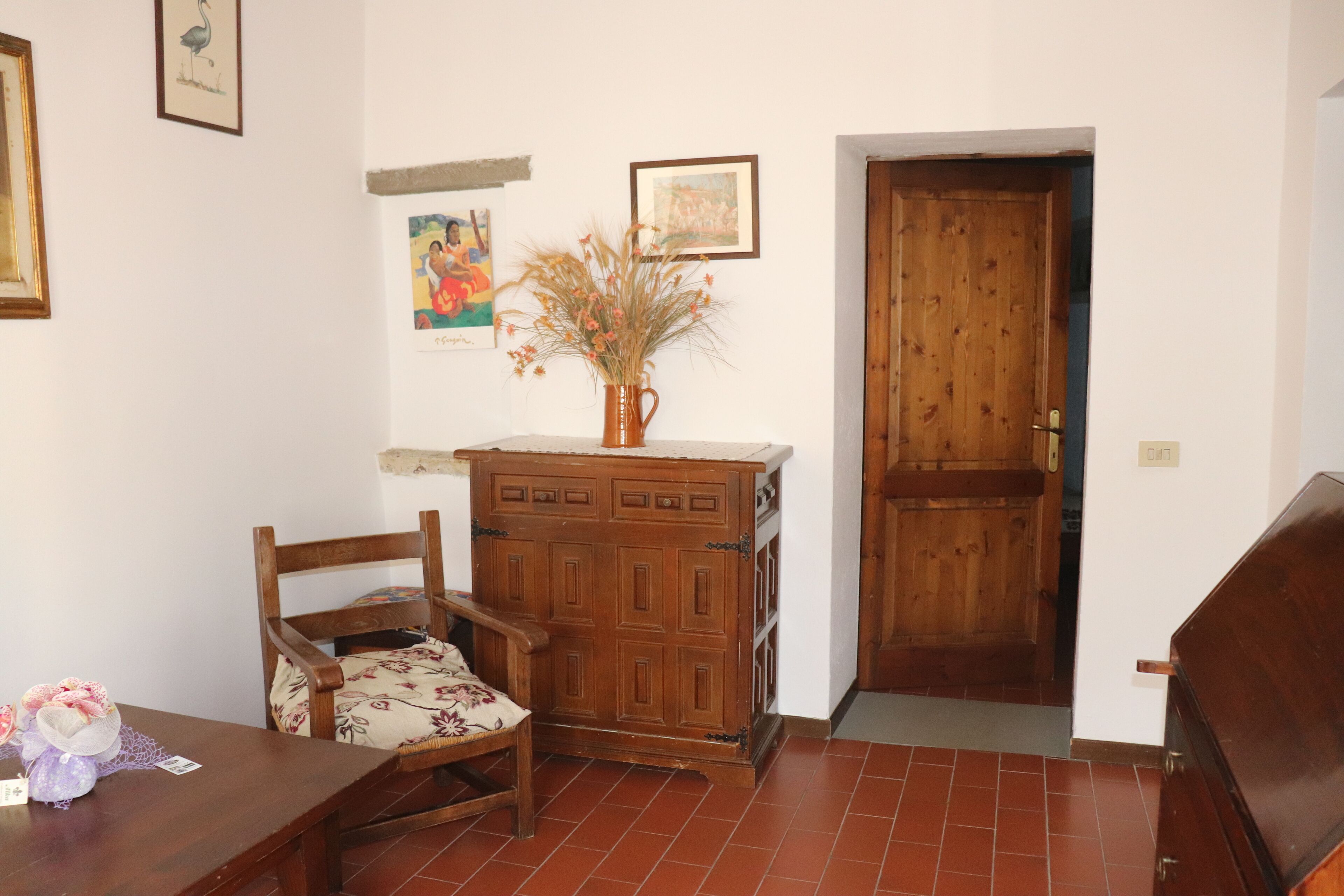 Quarto com um armário de madeira, uma cadeira, uma porta de madeira e piso de azulejos.