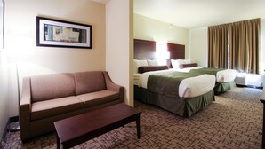 Quarto de hotel com sofá, uma cama de solteiro, uma cama de casal, um quadro na parede e uma janela com cortinas.