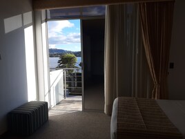 Quarto de hotel com uma cama, vista para um lago e varanda com guarda-corpo.