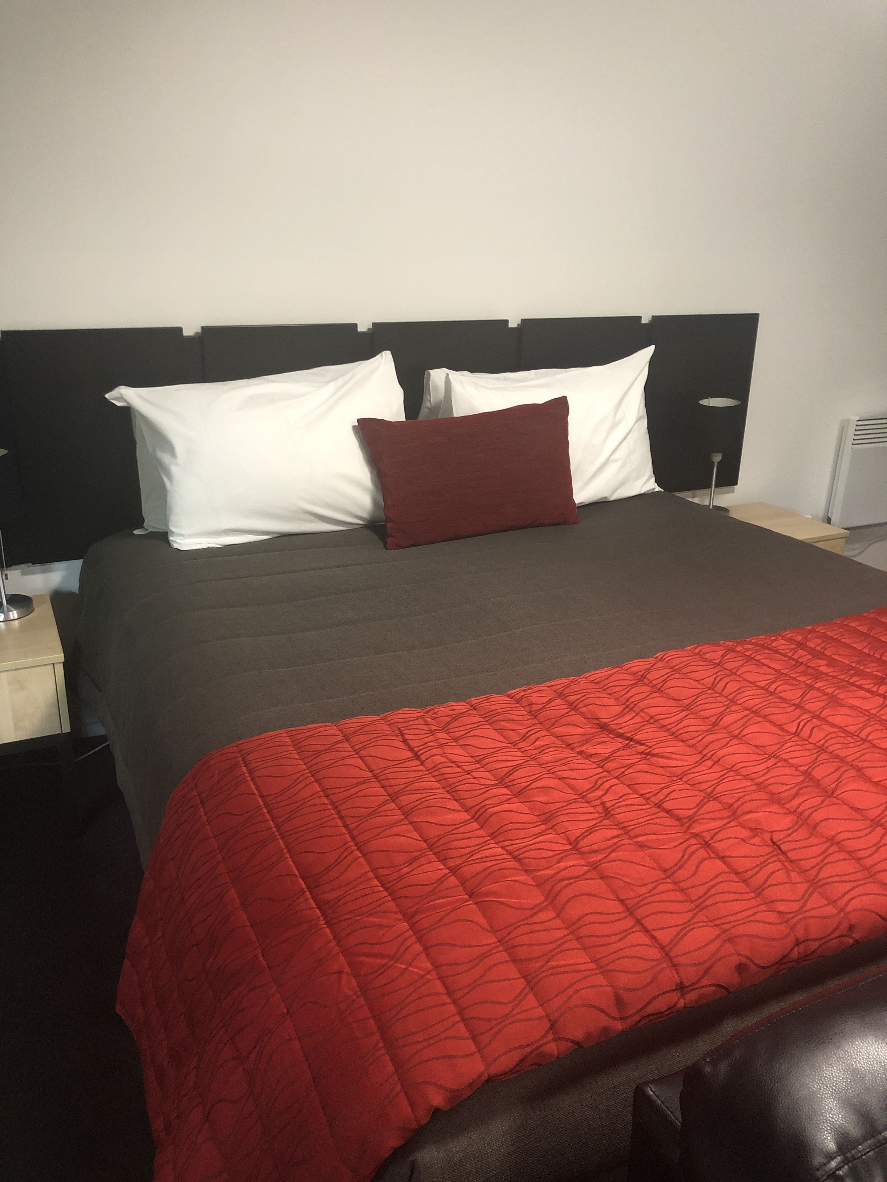 Uma cama com colcha vermelha, travesseiros brancos e cabeceira escura.