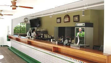 Uma área de bar com balcão, prateleiras com garrafas, uma televisão e um frigorífico.