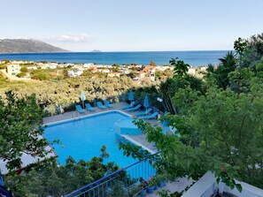 Área de piscina com água azul, cercada por vegetação e com vista para uma cidade costeira.
