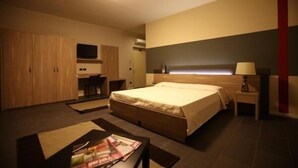 Quarto de hotel moderno com uma cama grande, uma escrivaninha, uma televisão e um guarda-roupa.