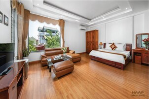Quarto de hotel moderno com sofá, mesa de centro de vidro, cama de madeira e televisão.