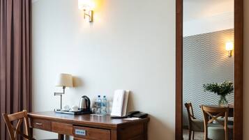 Quarto de hotel com uma escrivaninha de madeira, uma cadeira, um espelho, um abajur e uma cama.