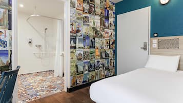 Quarto de hotel com uma cama, chuveiro, parede decorada com cartazes de viagens e piso estampado.