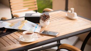 Uma mesa de madeira com um mapa, um smartphone, uma chávena de café, uma tigela de chocolates e um pequeno recipiente branco.
