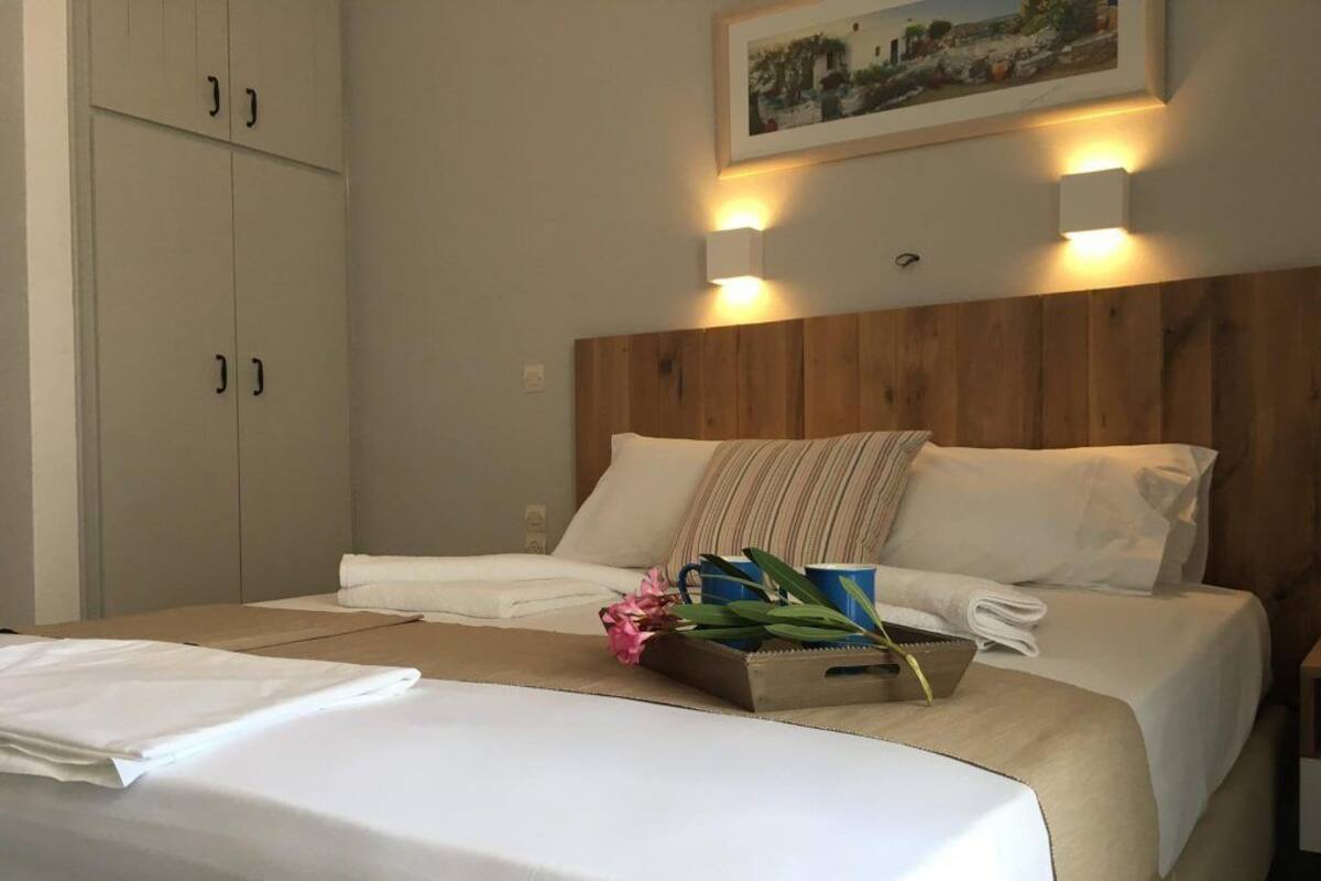 Quarto de hotel com duas camas, cabeceira de madeira, um quadro na parede e uma bandeja com flor e caneca sobre a cama.