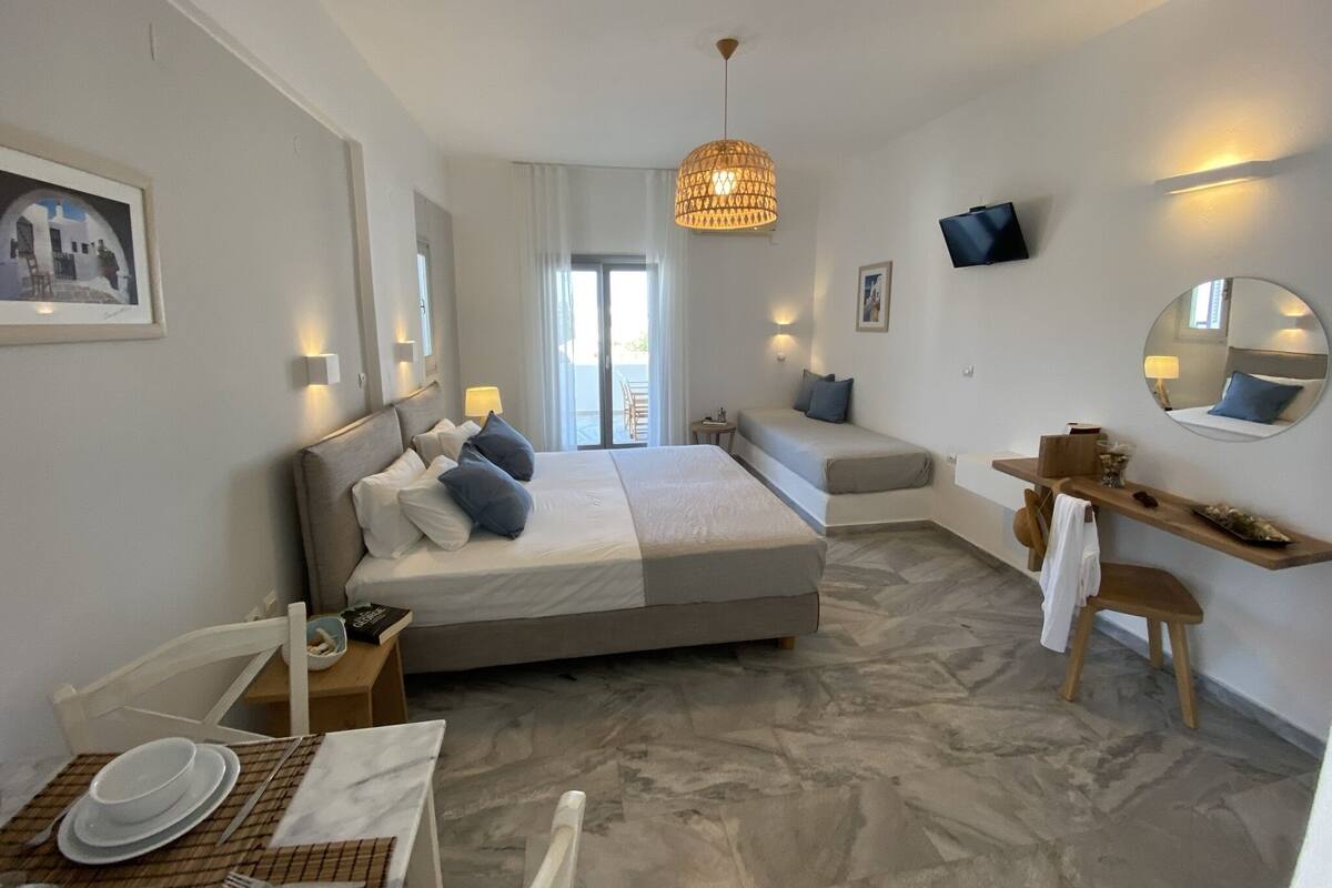 Quarto de hotel moderno com uma cama grande, área de jantar e varanda com vista.