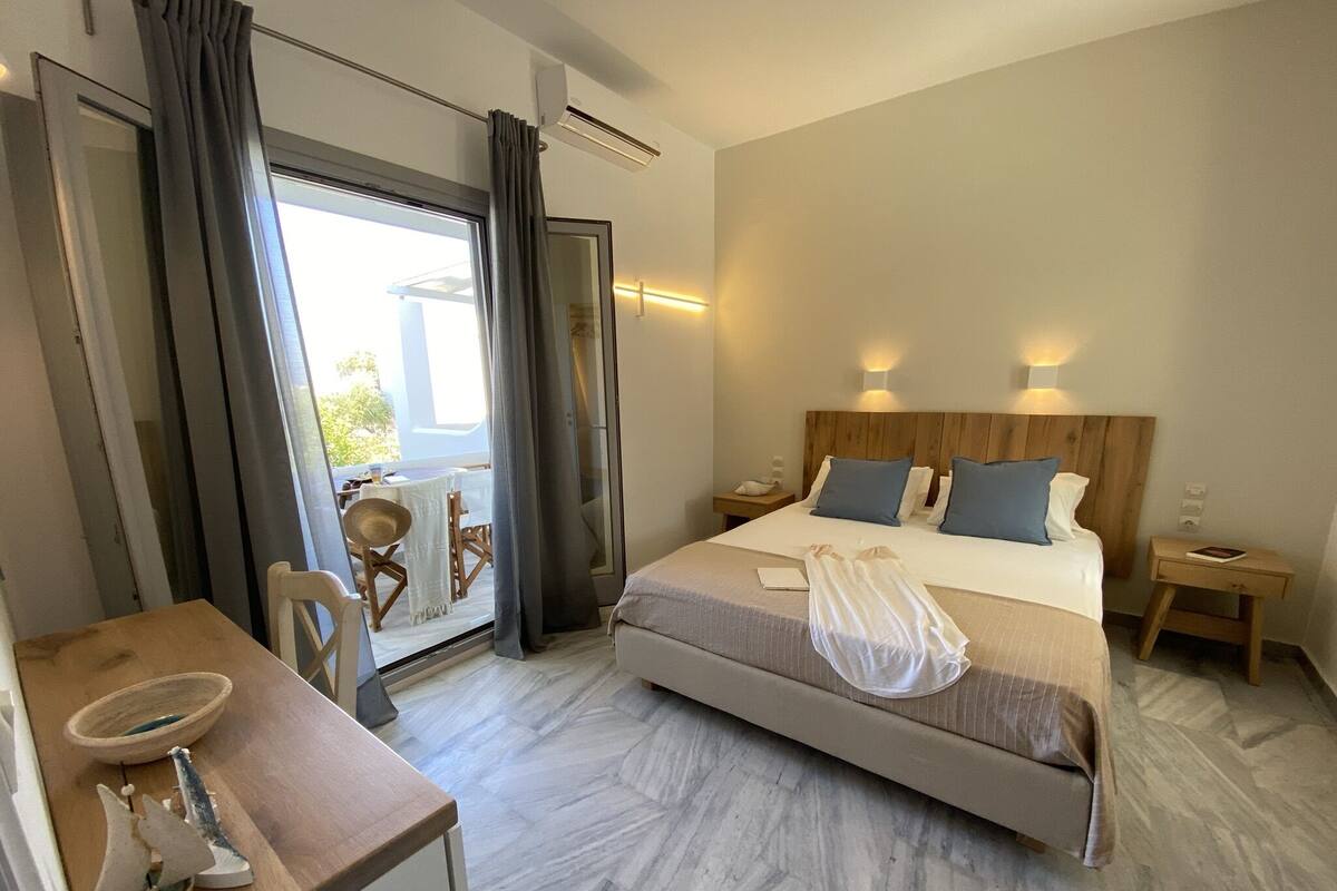 Quarto de hotel com cama, mesas de cabeceira, escrivaninha com tigela e decoração de peixe, e vista para o exterior.