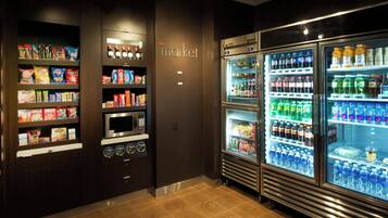Espaço com máquina de vendas de lanches, micro-ondas e refrigeradores de bebidas.