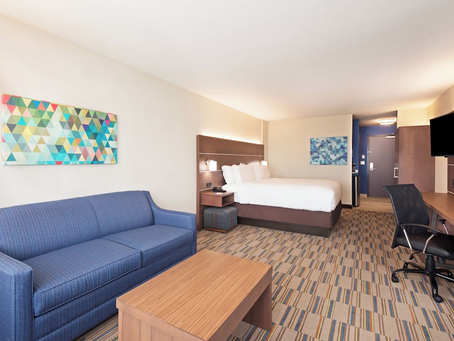 Quarto de hotel com cama, sofá azul, mesa de madeira, escrivaninha e televisão.