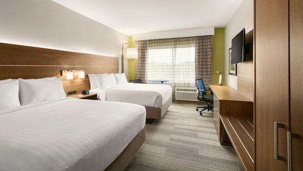 Quarto de hotel com duas camas, uma escrivaninha, uma cadeira, uma televisão e uma janela com cortinas.
