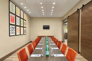 Uma sala de conferência com uma mesa comprida, cadeiras laranja e quadros na parede.