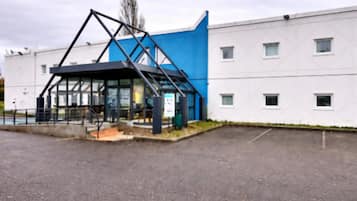 Um edifício moderno com fachada azul e branca, entrada coberta e estacionamento.