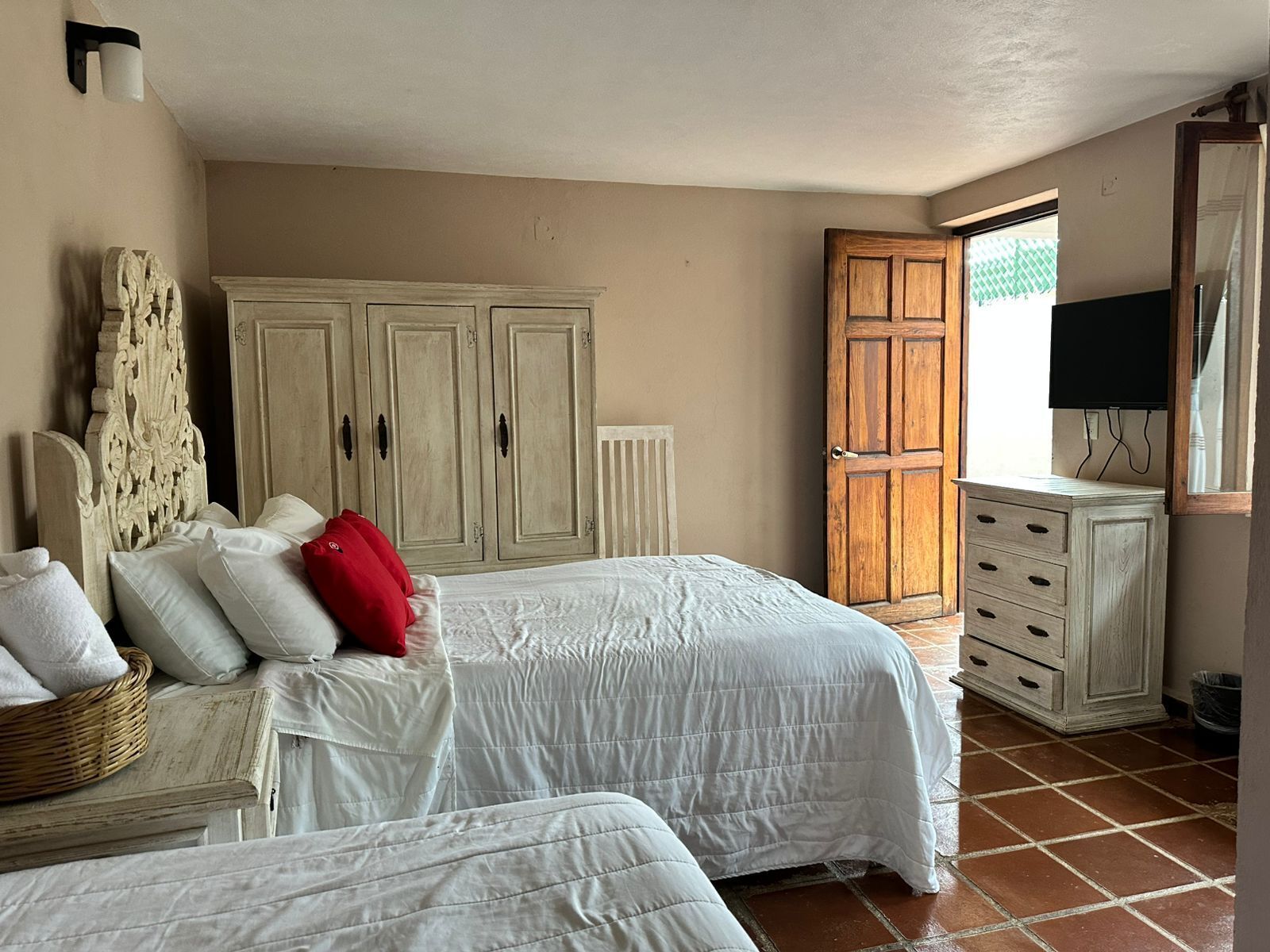 Quarto com duas camas, cômoda, guarda-roupa e televisão.