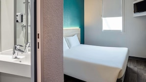 Quarto de hotel com cama, banheiro com chuveiro, televisão fixada na parede e janela.