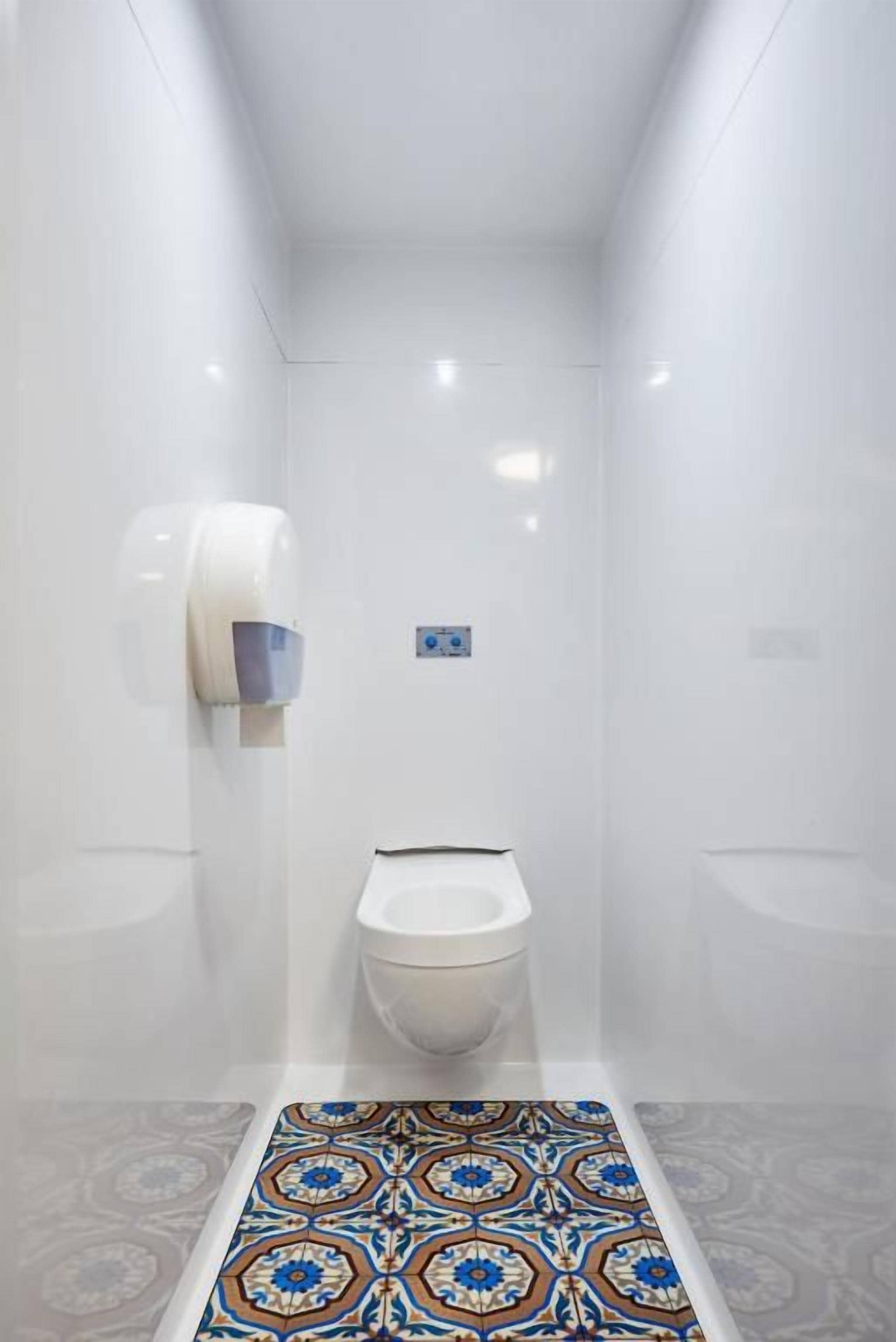 Casa de banho pequena e fechada, com sanita, secador de mãos e pavimento estampado.
