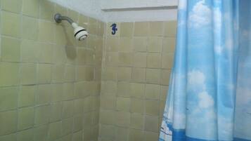 Um banheiro com paredes revestidas de azulejos bege, chuveiro com um chuveiro manual branco e cortina de chuveiro azul com padrão de nuvens.