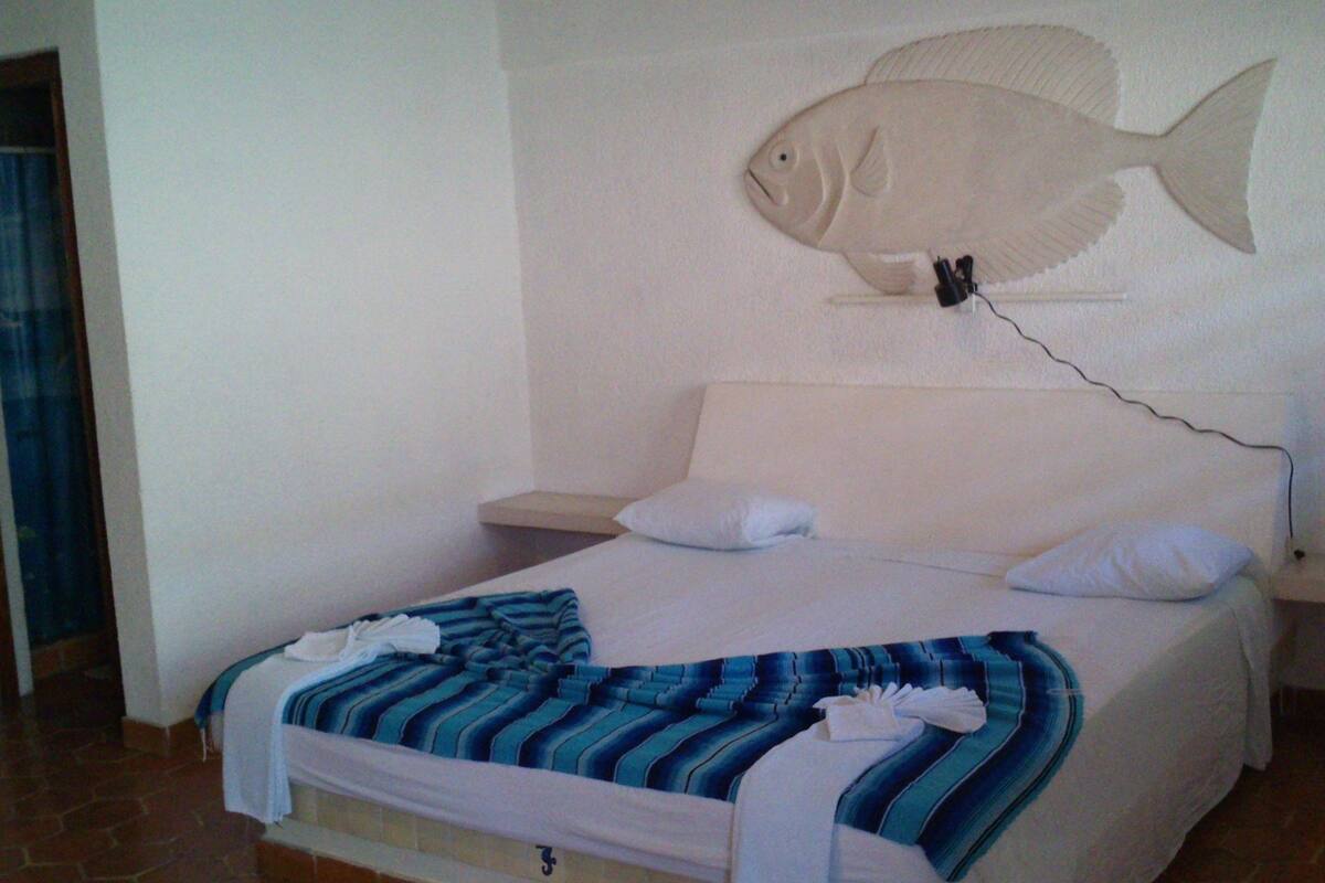 Uma cama com cobertor listrado, almofadas e uma decoração de parede em formato de peixe.