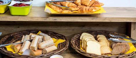 Um buffet de café da manhã com diversos pães, doces e bebidas.
