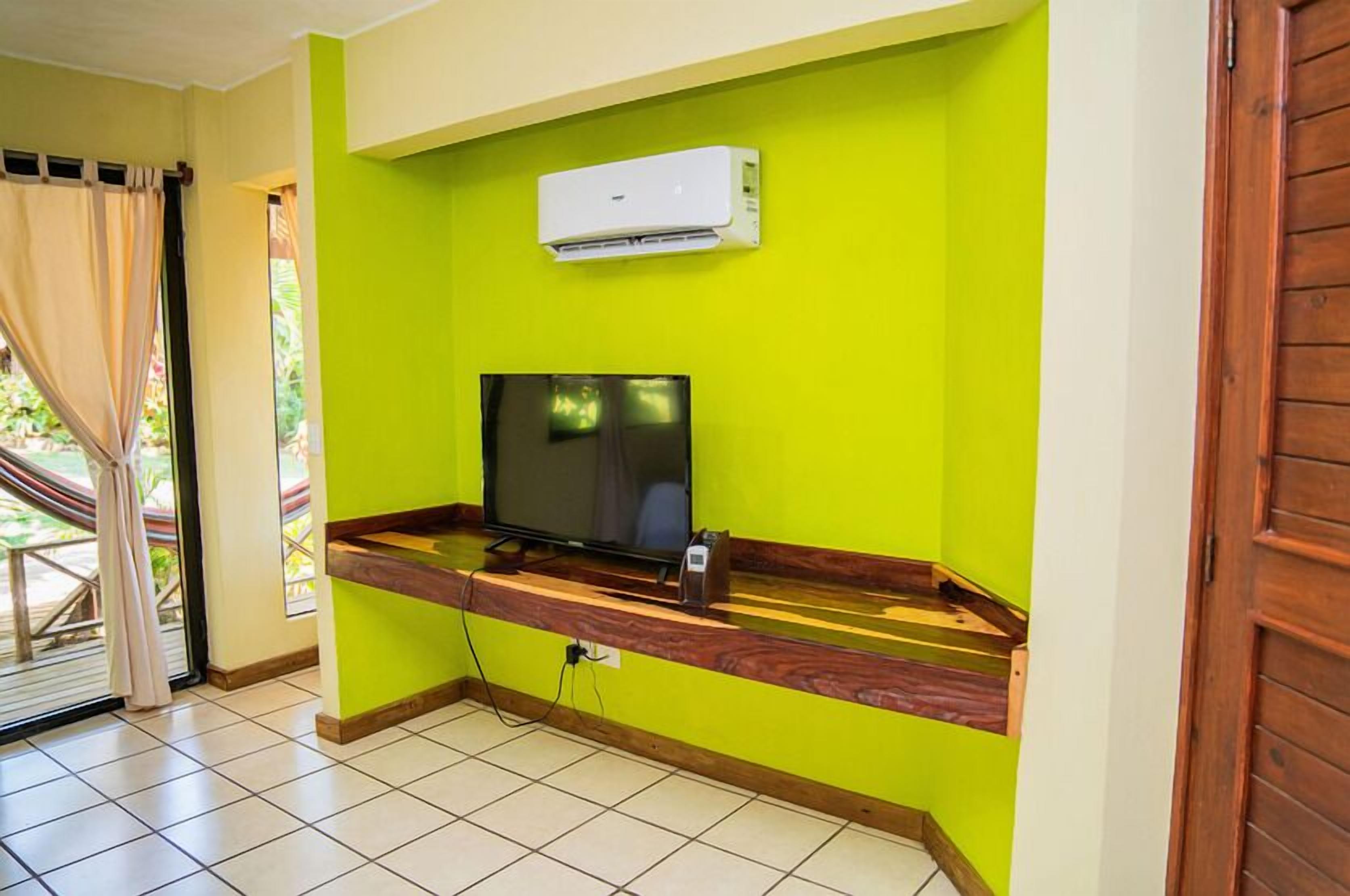 Quarto com televisão numa prateleira de madeira, ar condicionado na parede e chão em mosaico.
