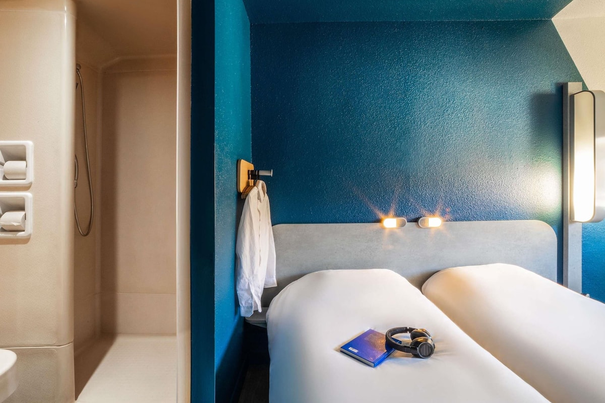 Quarto de hotel moderno com chuveiro, cama com travesseiro, um livro e fones de ouvido.