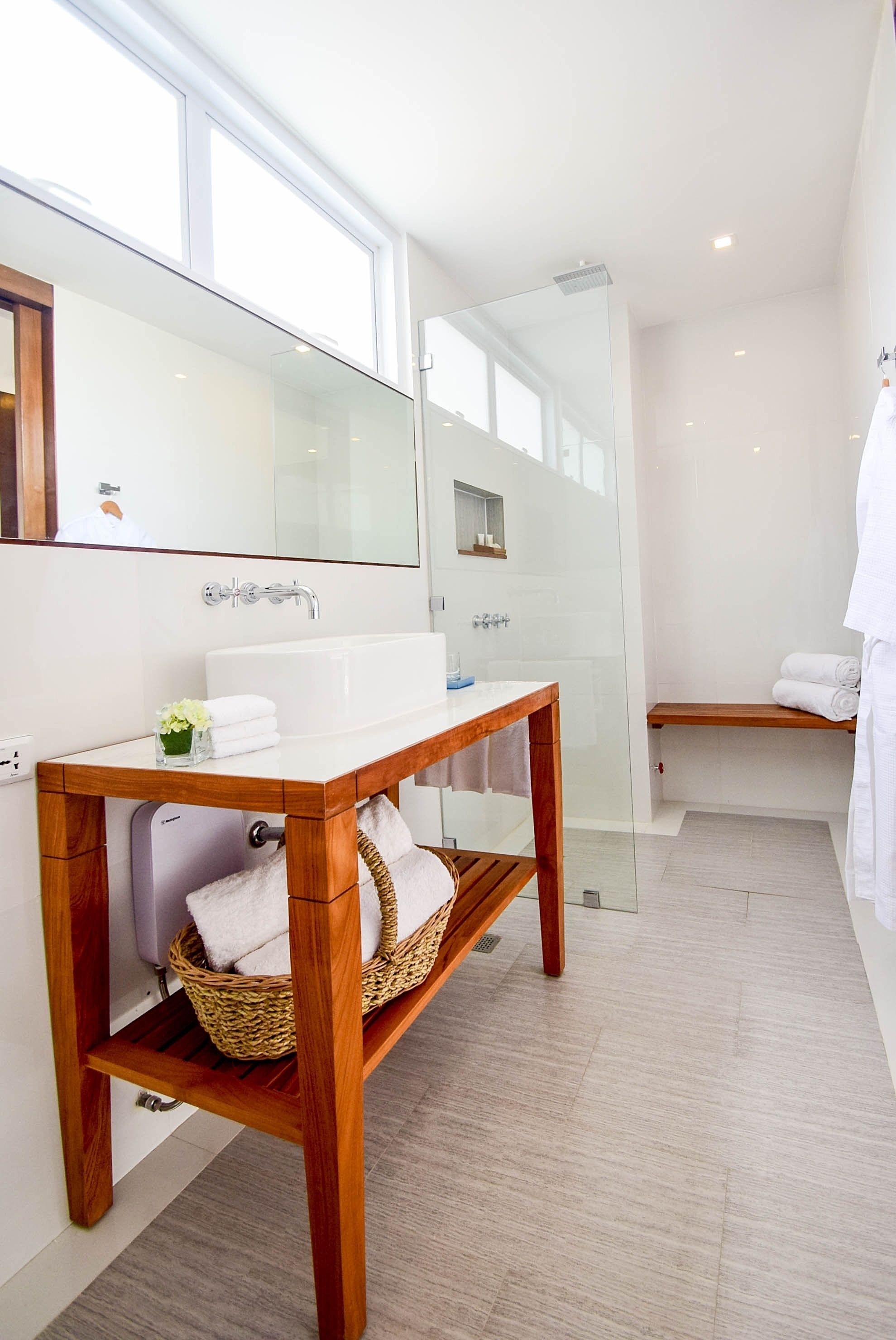 Uma casa de banho moderna com um espelho grande, lavatório branco e toucador de madeira.