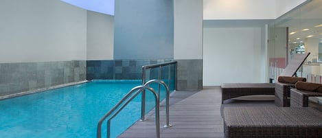 Uma piscina com deck de madeira e área de estar com móveis de vime.