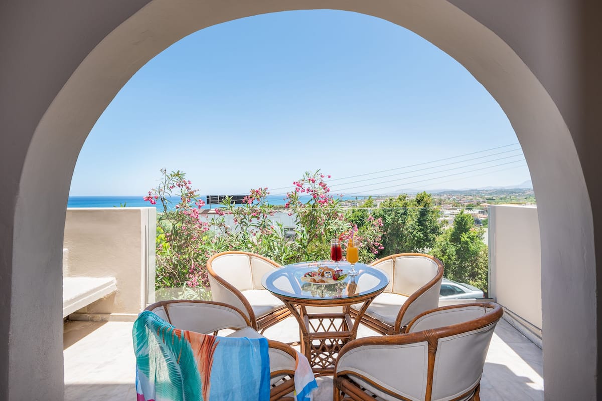 Uma varanda com mesa e cadeiras, oferecendo uma vista panorâmica do mar e do verde.