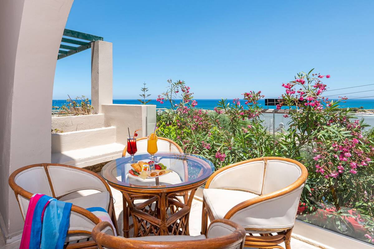 Uma varanda com cadeiras de vime, uma mesa de vidro com café da manhã e vista para o mar.