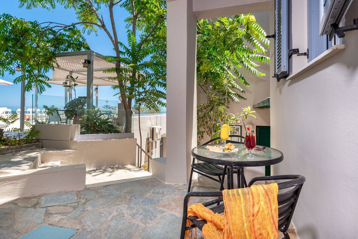Um pátio com mesa, cadeiras e tampo de vidro. Possui área de estar coberta com pérgola e vista para o mar.