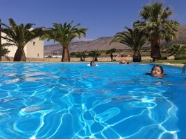 Piscina com águas cristalinas azuis, rodeada por palmeiras e ao fundo, montanhas.
