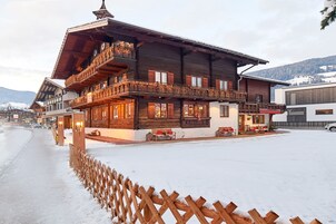 Um chalé de madeira tradicional com varandas, uma área de estar coberta ao ar livre e uma rua coberta de neve.