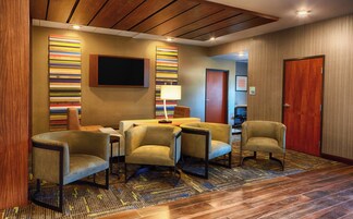 Quarto de hotel com teto de madeira, televisão de tela plana, escrivaninha com luminária e quatro cadeiras.