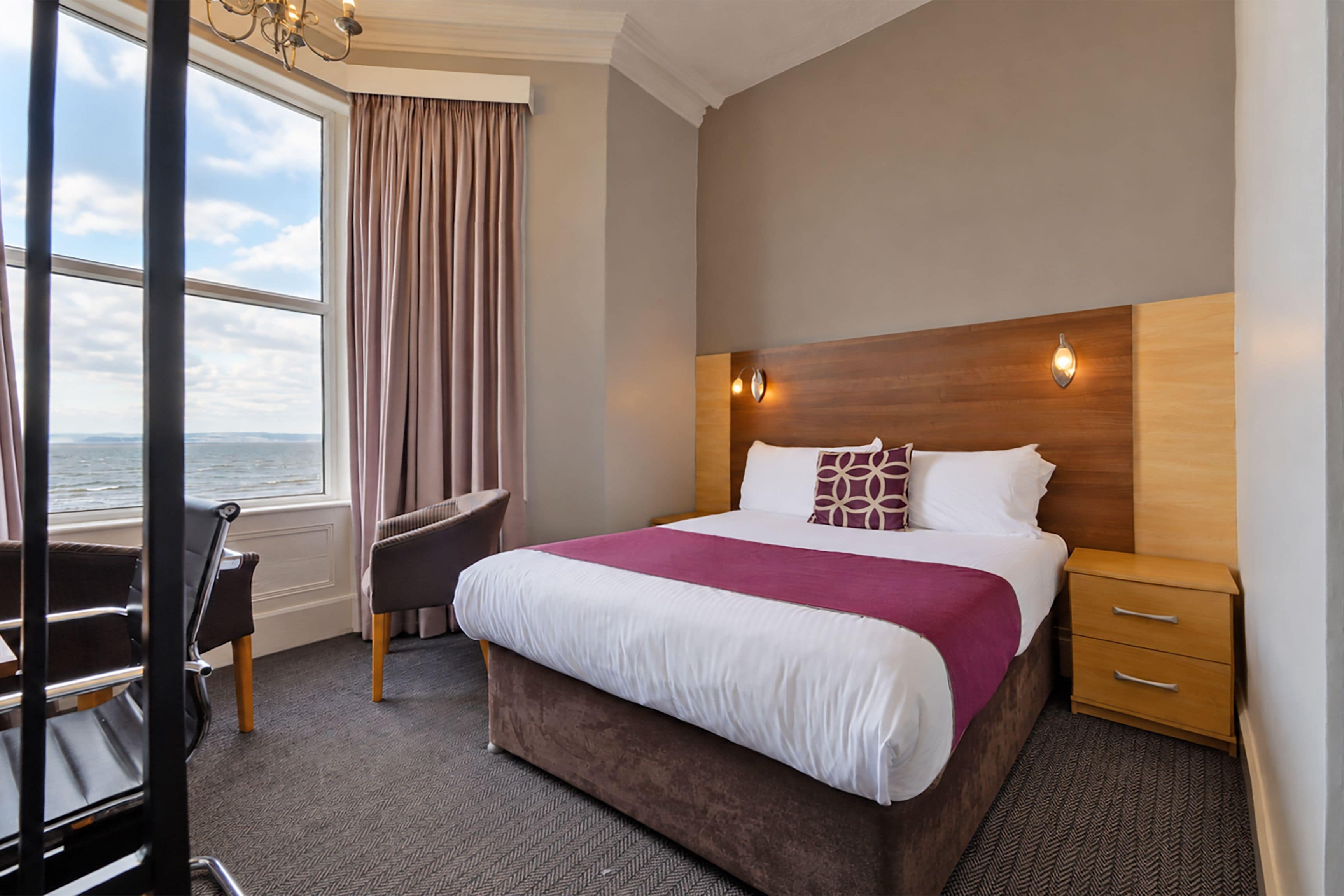 Quarto de hotel com uma cama grande, uma escrivaninha e vista para o mar.